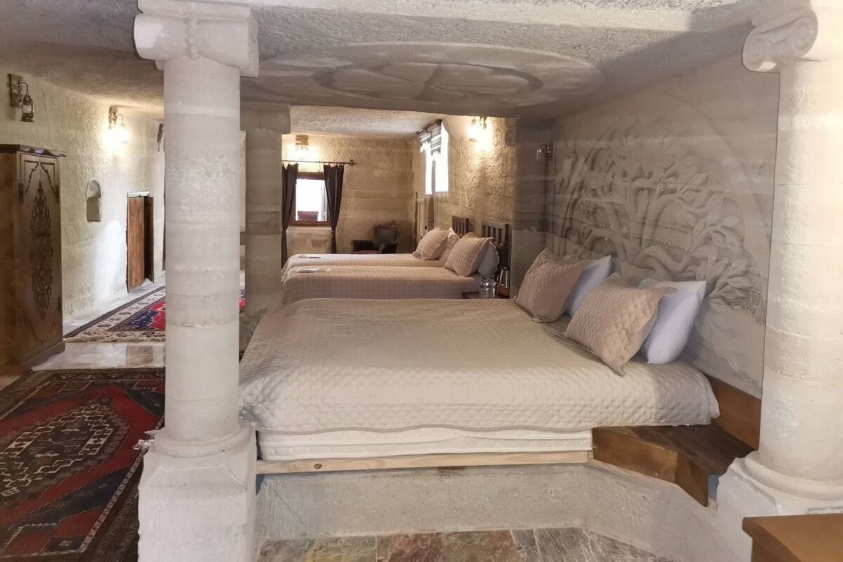 Quarto com duas camas, um armário de madeira, tapete estampado e parede de pedra com esculturas.