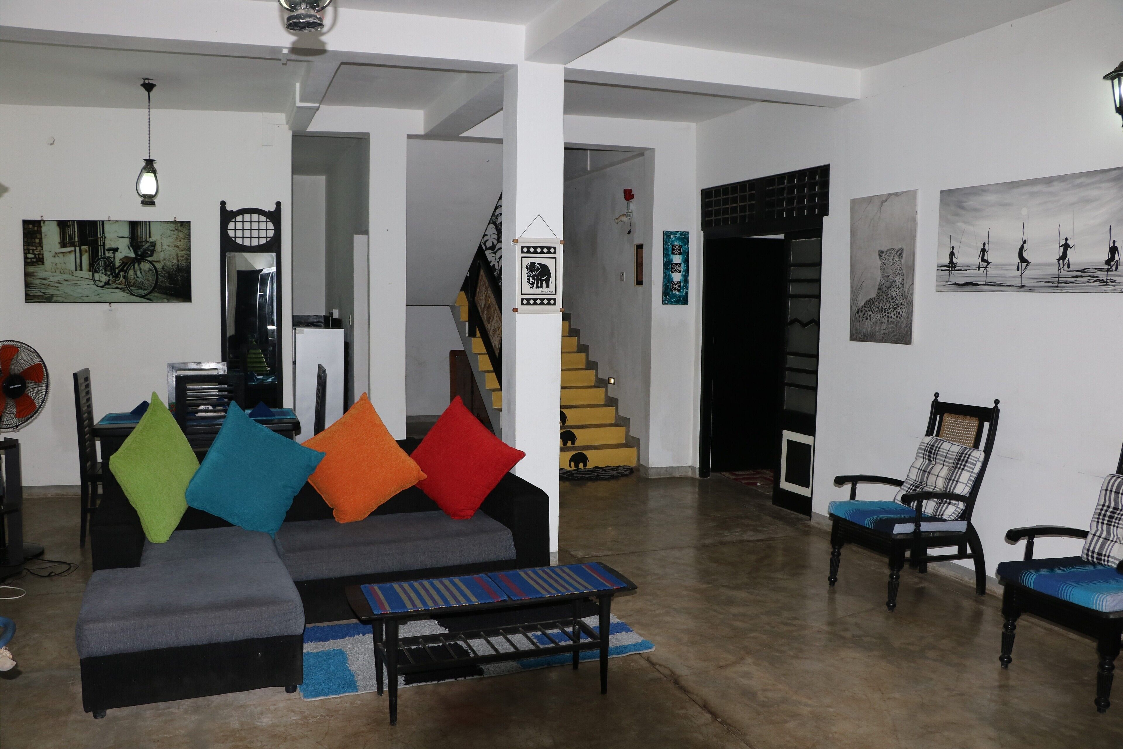Uma sala de estar com sofá, mesa de centro e duas cadeiras. Escada leva a outro andar.