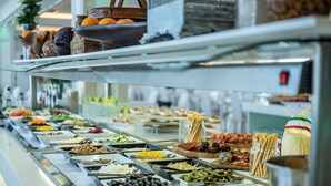 Buffet com diversas opções de comida, incluindo frutas, queijos e carnes.