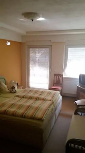 Quarto de hotel com cama, poltrona, escrivaninha e televisão.