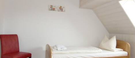Quarto com cama de madeira, uma cadeira vermelha e teto inclinado com claraboia.