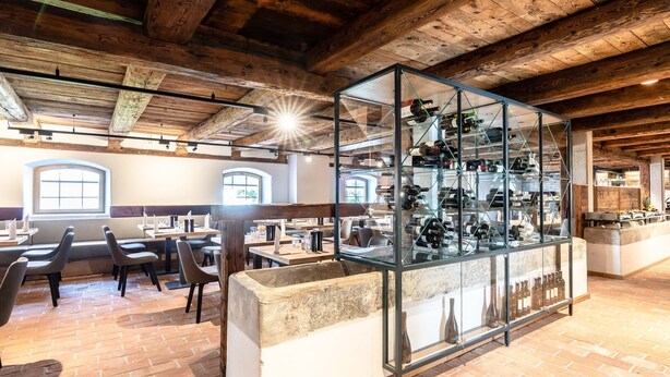 Um interior rústico com vigas de madeira aparente, uma vitrine de vidro com garrafas e chão de tijolos.