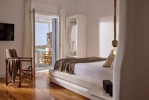 Quarto com cama, cadeira, televisão e vista para o exterior.