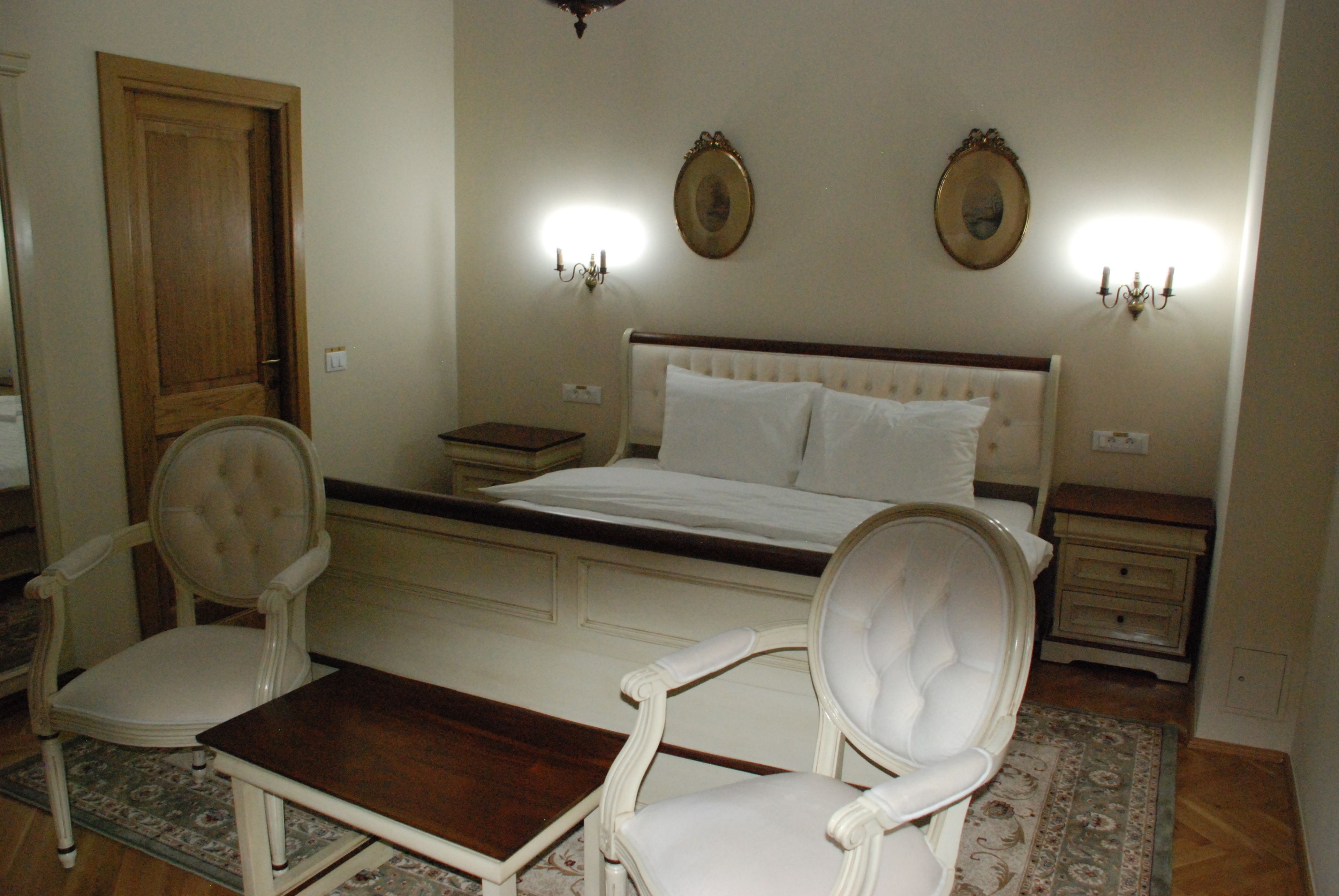 Quarto com cama, duas mesas de cabeceira, uma mesa de madeira, duas poltronas estofadas e um tapete estampado.