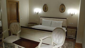 Quarto com cama, duas mesas de cabeceira, uma mesa de madeira, duas poltronas estofadas e um tapete estampado.