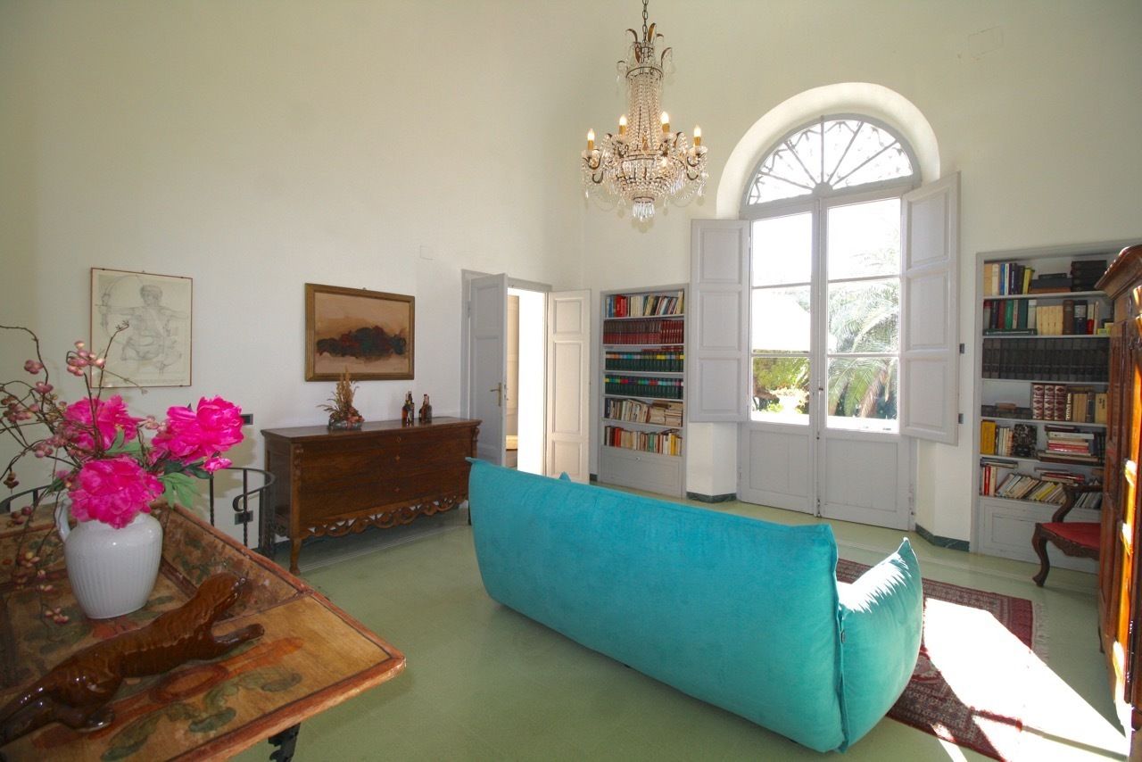 Um quarto espaçoso com uma janela grande, um candelabro, uma estante de livros e um sofá.