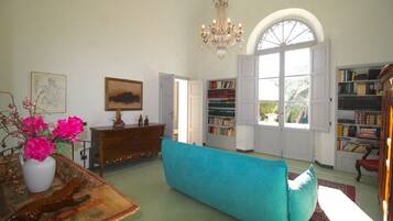 Um quarto espaçoso com uma janela grande, um candelabro, uma estante de livros e um sofá.
