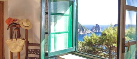 Quarto com uma grande janela que oferece vista para a costa rochosa e o mar.