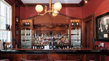 Um bar com balcão de madeira, várias garrafas, copos e um lustre.