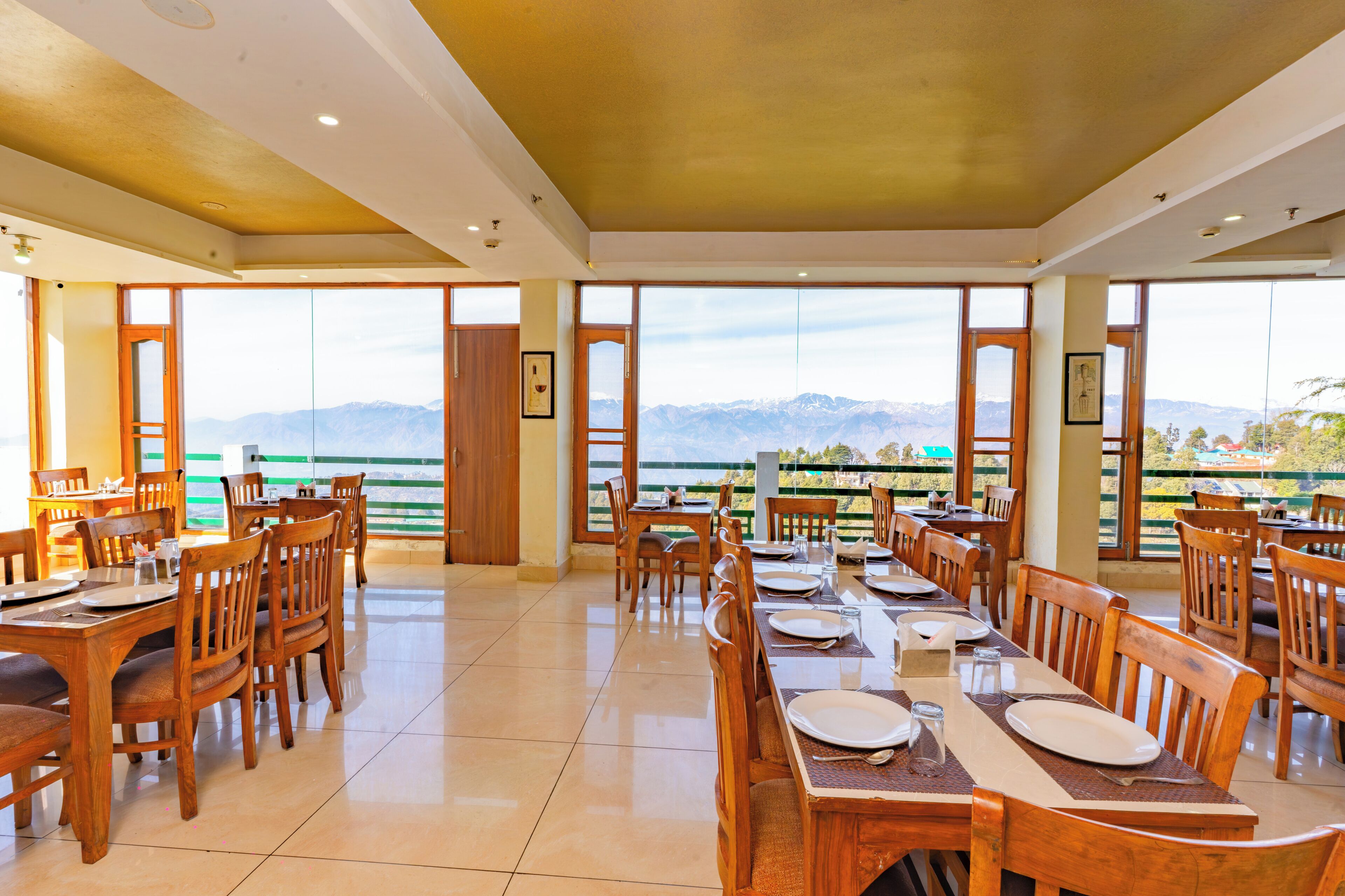 Restaurante com mesas e cadeiras de madeira, janelas amplas com vista para a montanha e piso de azulejos.