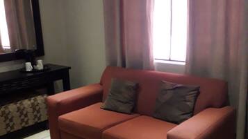 Uma sala de estar com um sofá, uma mesa pequena com um espelho e uma janela com cortinas.