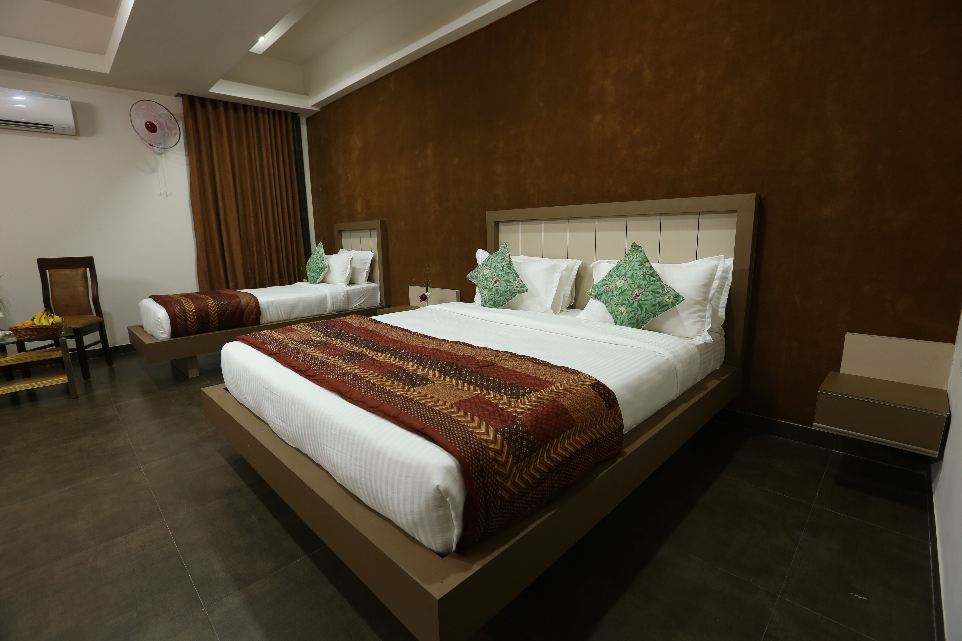 Quarto de hotel com cama grande, mesa de cabeceira, uma cadeira e um espelho.