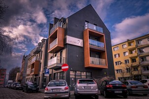 Um edifício moderno com varandas, um aviso de proibido estacionar e carros estacionados.