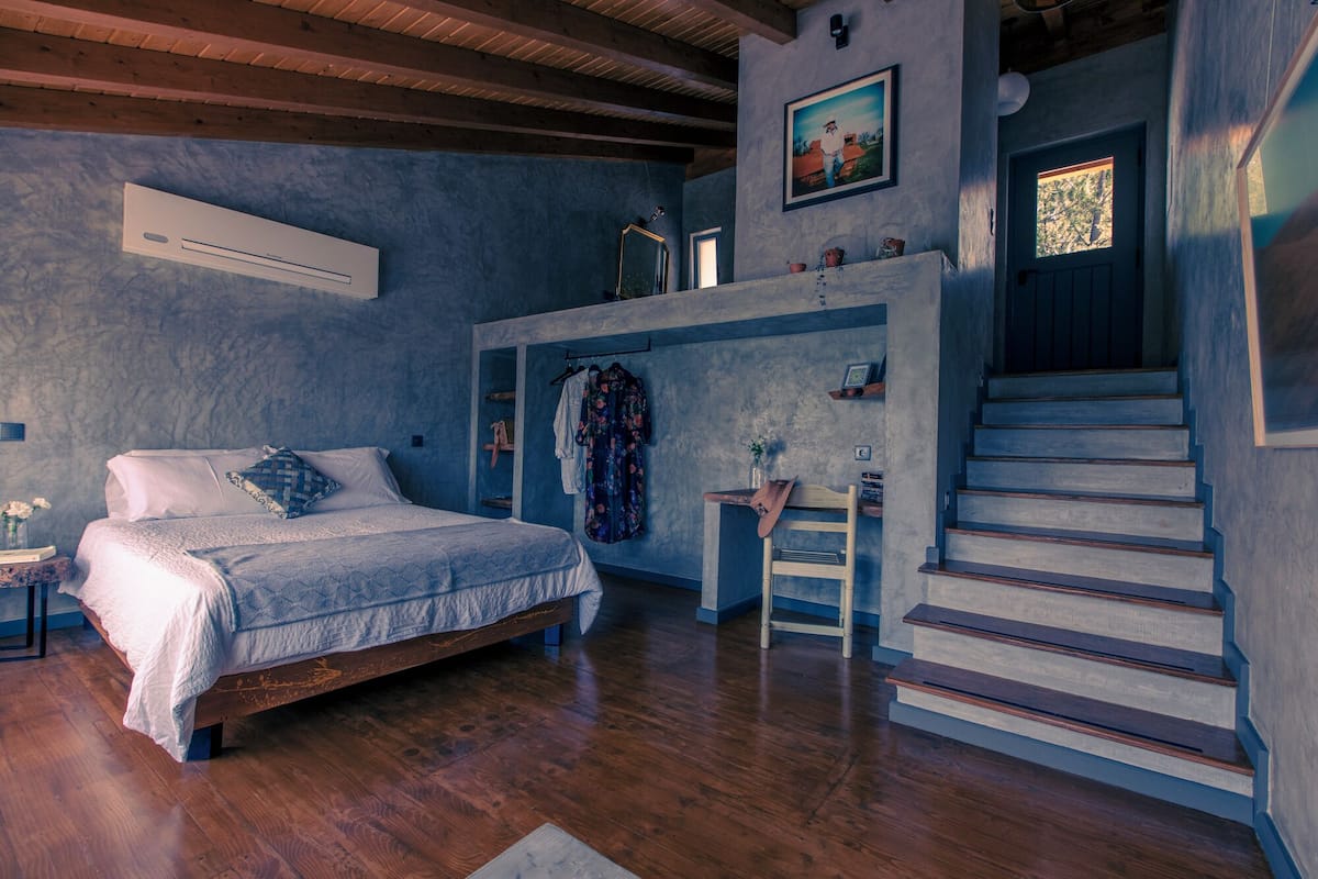Quarto com cama de madeira, uma pequena mesa, uma cadeira e escada.