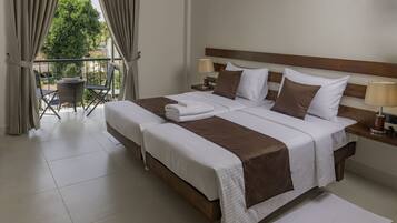 Uma cama de casal com cabeceira de madeira, duas mesas de cabeceira com luminárias e uma varanda com mesa e cadeiras.