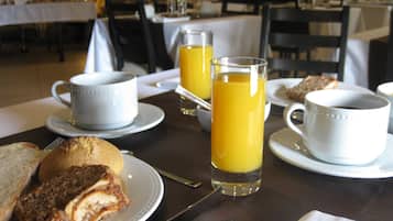 Uma mesa de café da manhã com pratos de comida, copos de suco de laranja e xícaras brancas.