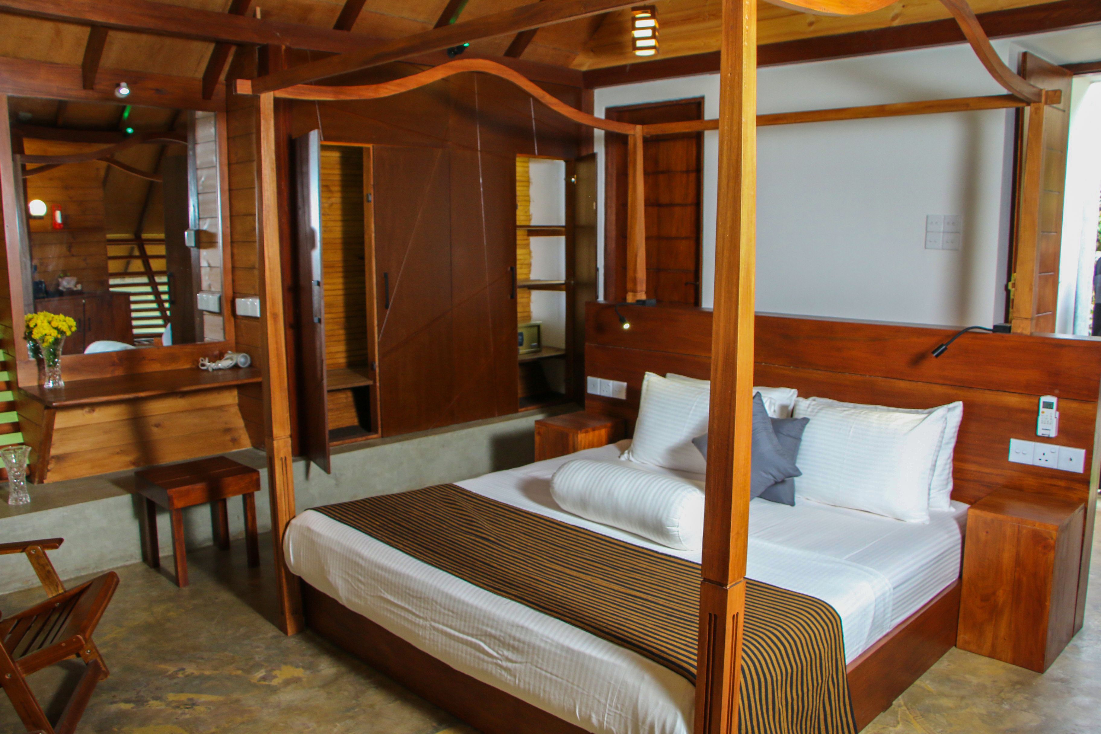 Uma cama de madeira com dossel, roupa de cama branca, um criado-mudo de madeira e um espelho na parede.