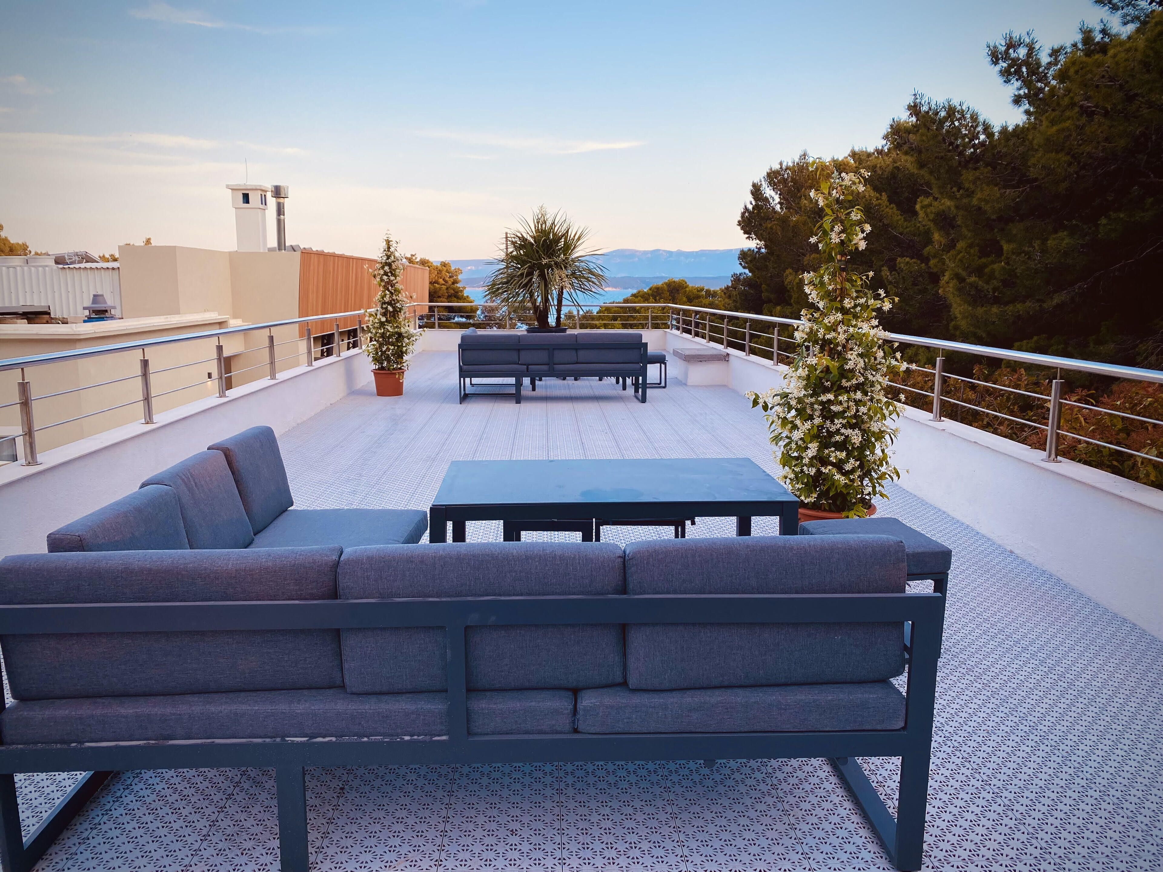 Terraço no telhado com um sofá cinza, uma mesa e plantas em vasos.