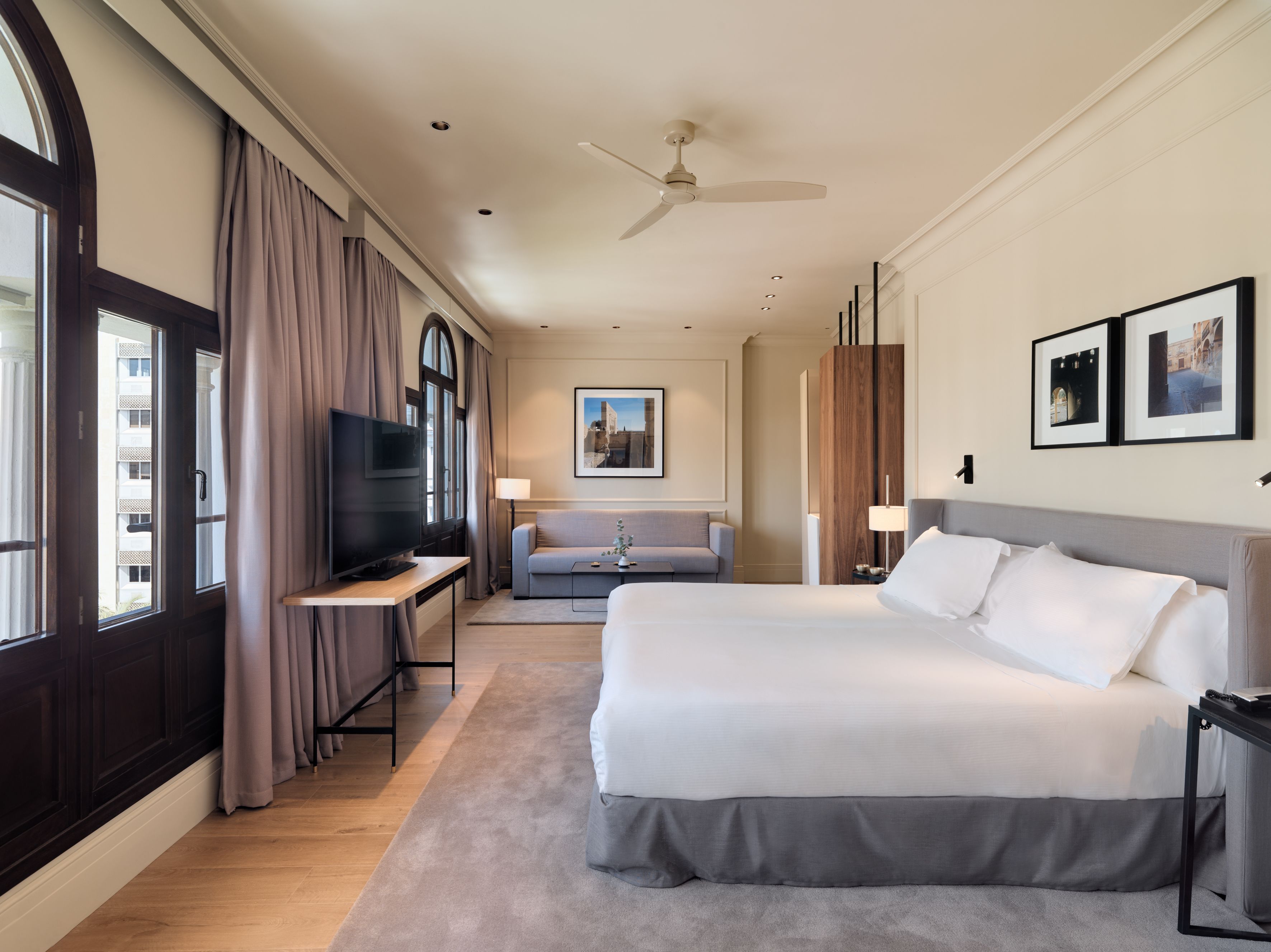 Quarto de hotel moderno com uma cama grande, televisão, sofá e escrivaninha.