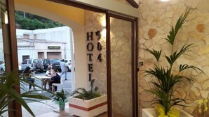 Entrada de um hotel com parede de pedra, uma placa indicando "HOTEL 4" e plantas em vasos.