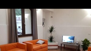 Uma sala de estar com dois sofás laranja, uma televisão, uma mesa pequena e uma planta.