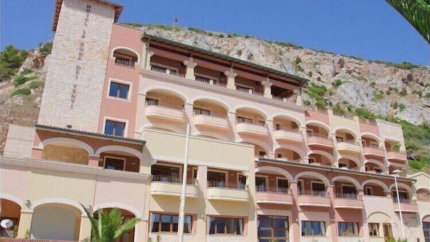 Um hotel com vários andares, varandas, fachada de pedra e montanhas ao fundo.