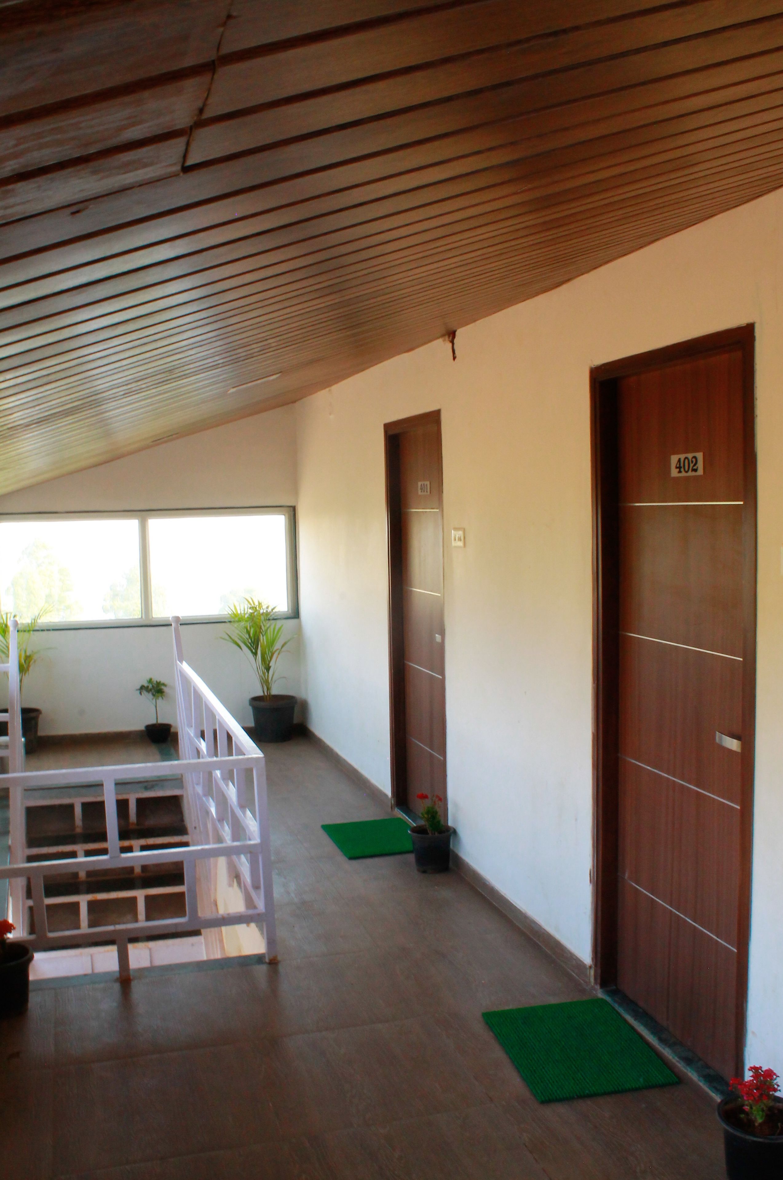 Um corredor com piso de madeira, plantas em vasos, corrimão branco e portas numeradas 402 e 403.