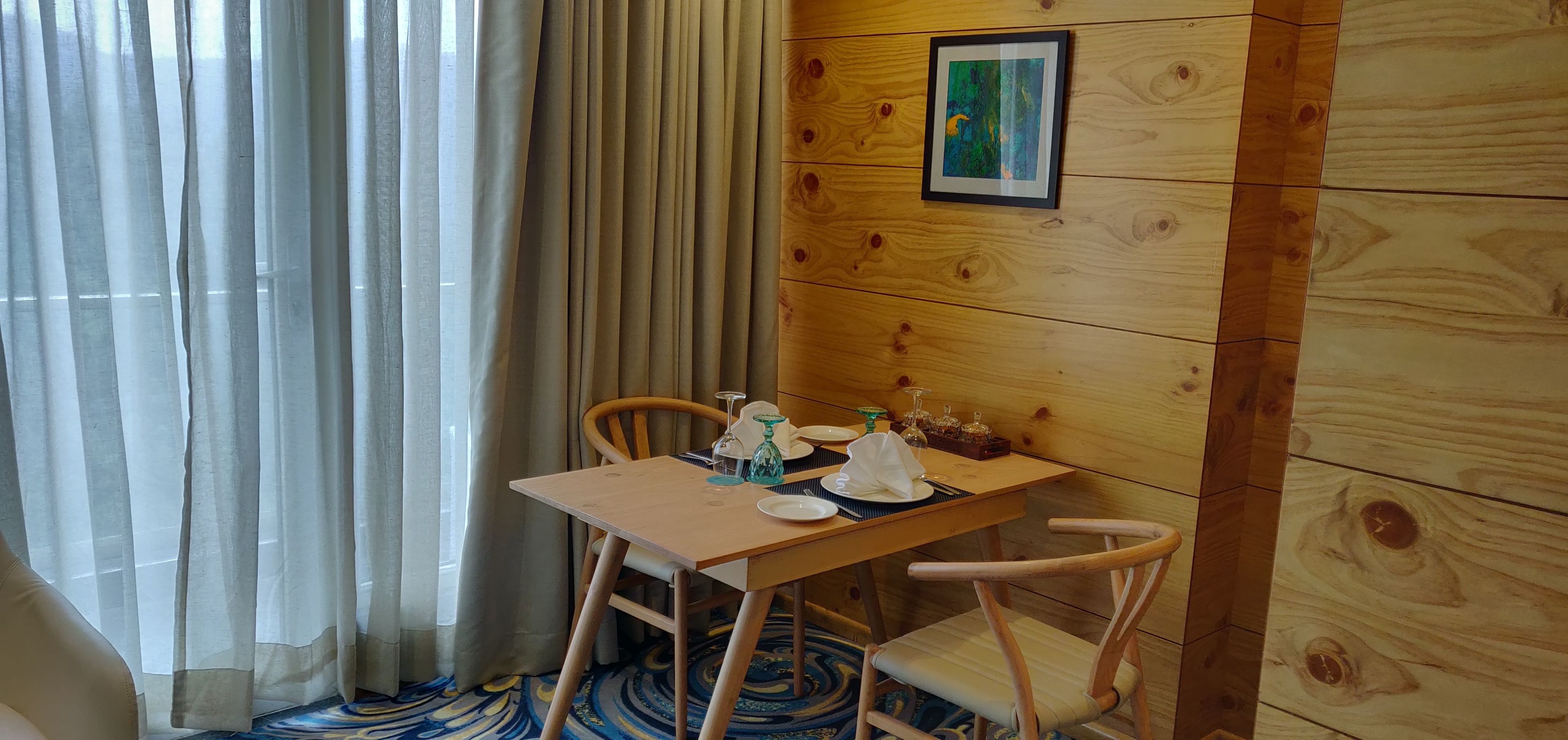 Um quarto com painéis de madeira, uma mesa de jantar posta para dois, uma cadeira e um quadro na parede.