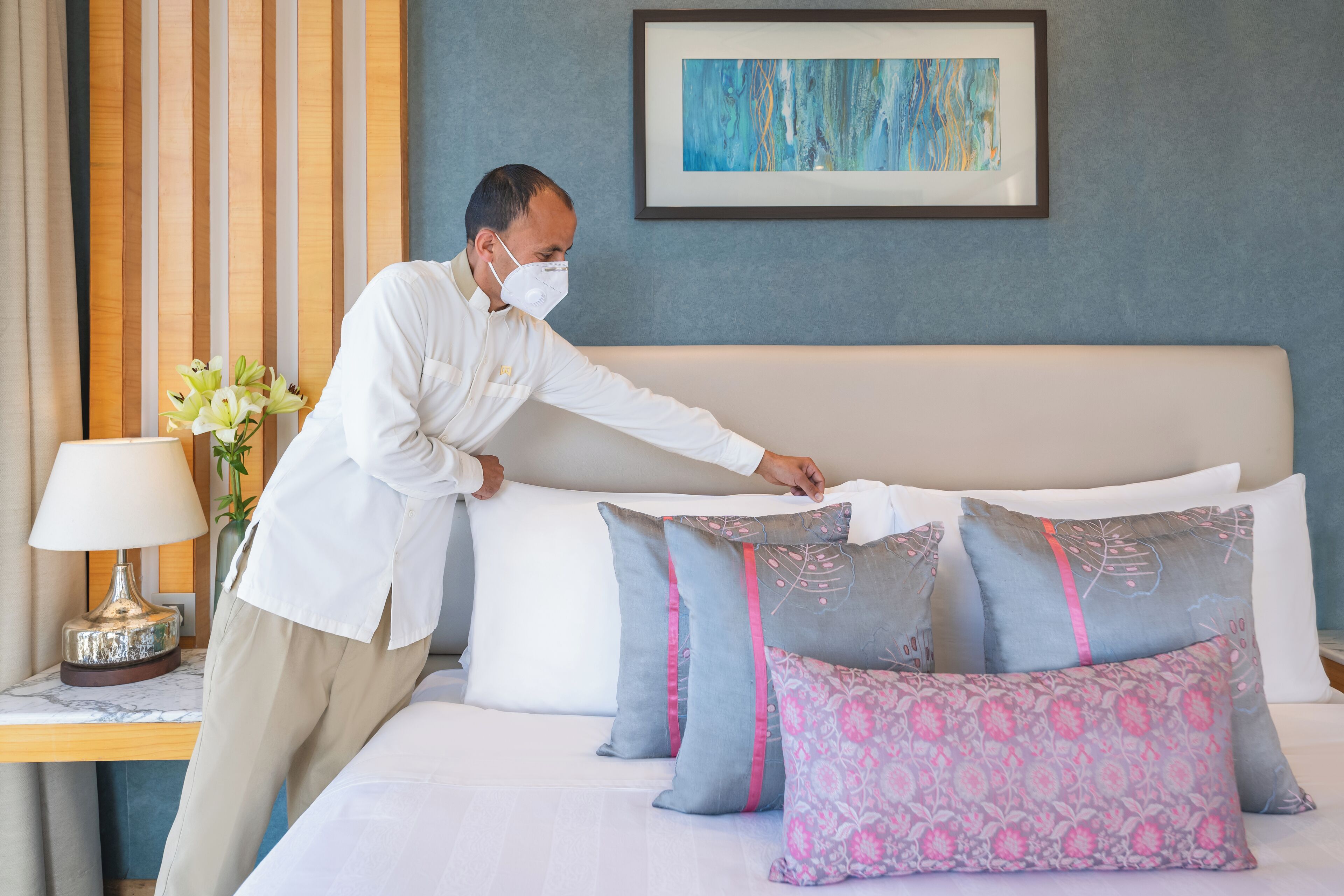 Quarto de hotel com cama bem arrumada, mesa de cabeceira com abajur e uma obra de arte emoldurada na parede.