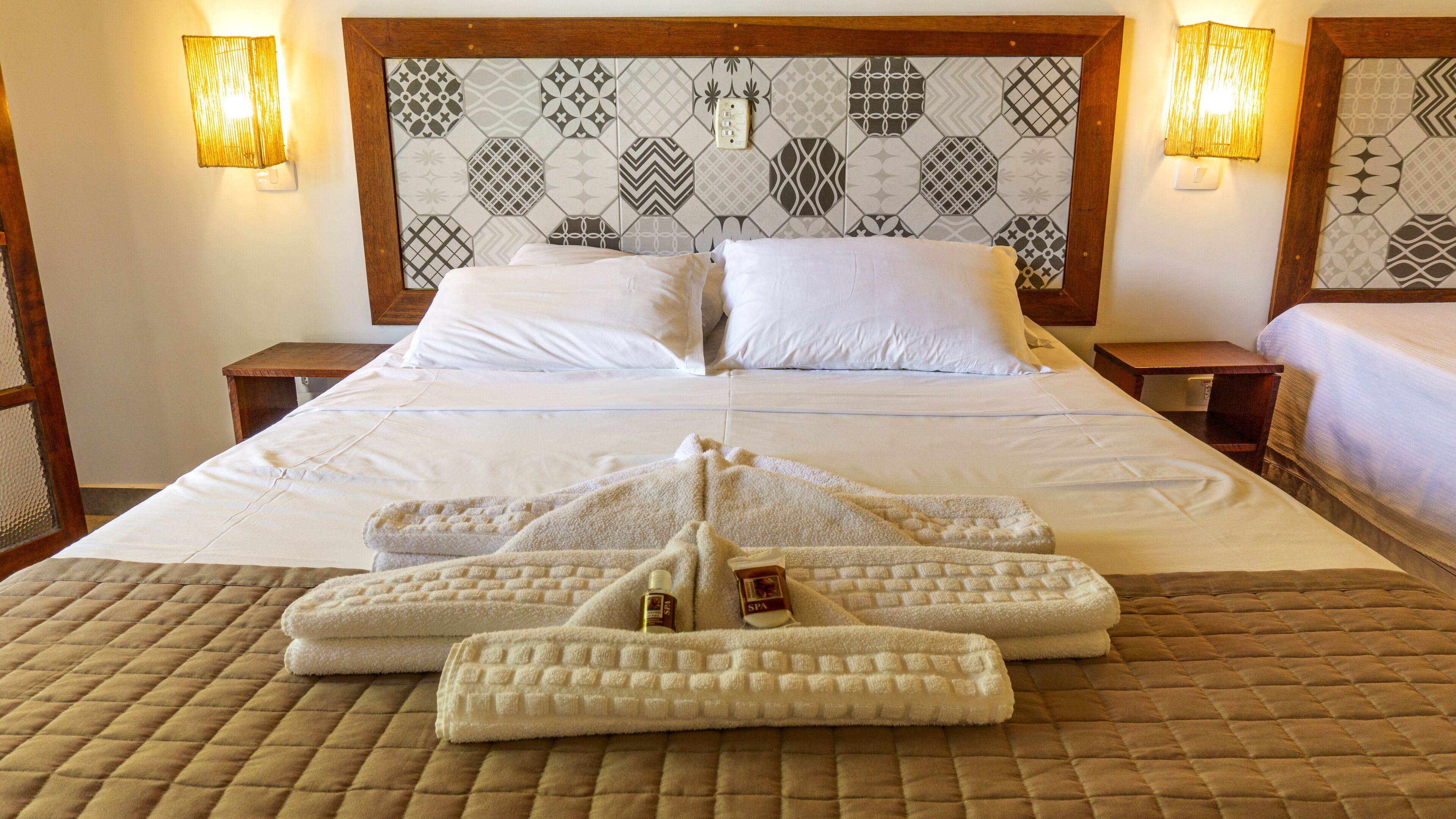 Quarto de hotel com uma cama grande, duas mesas de cabeceira e uma cabeceira com padrão geométrico de azulejos.