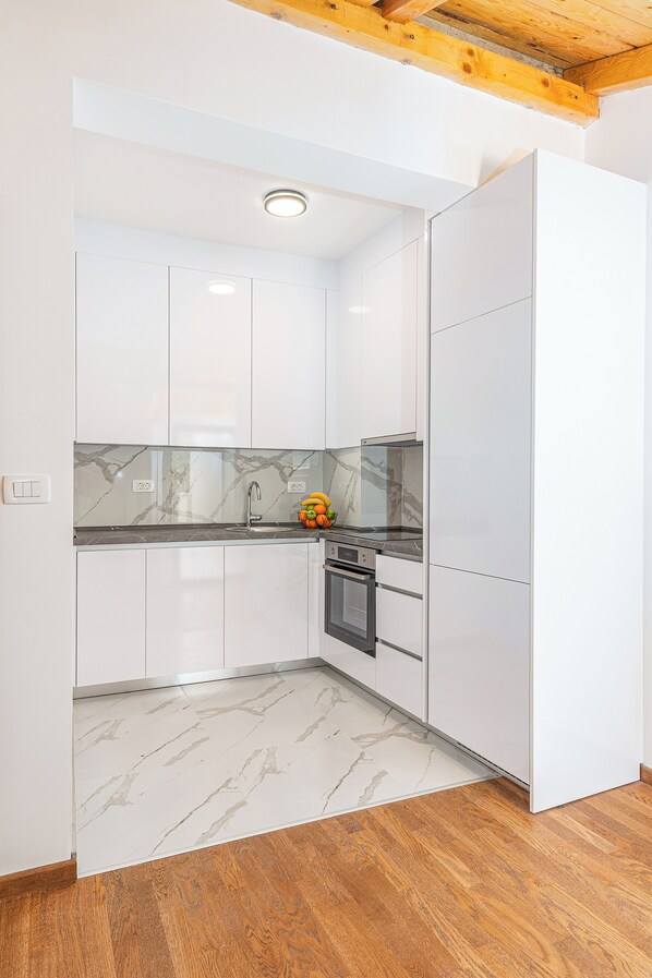 Uma cozinha moderna com armários brancos, painel de backsplash de mármore e teto de madeira.