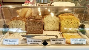 Uma vitrine com diversos tipos de pão caseiro, incluindo integral, do dia e de cenoura.
