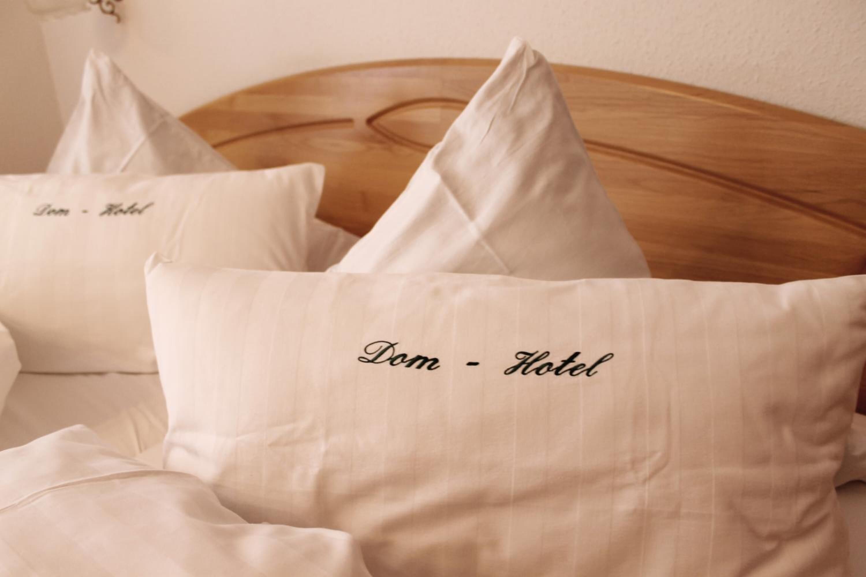 Cama com cabeceira de madeira e vários travesseiros, alguns com texto.
