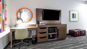 Quarto de hotel com secretária, cadeira, televisão, micro-ondas e gavetas.