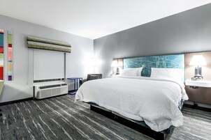 Quarto de hotel com uma cama grande, televisão de tela plana, escrivaninha com cadeira, luminária e banheiro com pia e espelho.