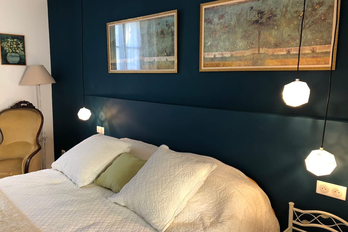 Quarto com uma cama, uma cadeira e duas pinturas na parede.