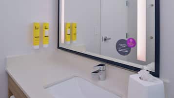 Uma casa de banho moderna com uma pia branca, um espelho e duas embalagens de sabonete líquido amarelo na parede.