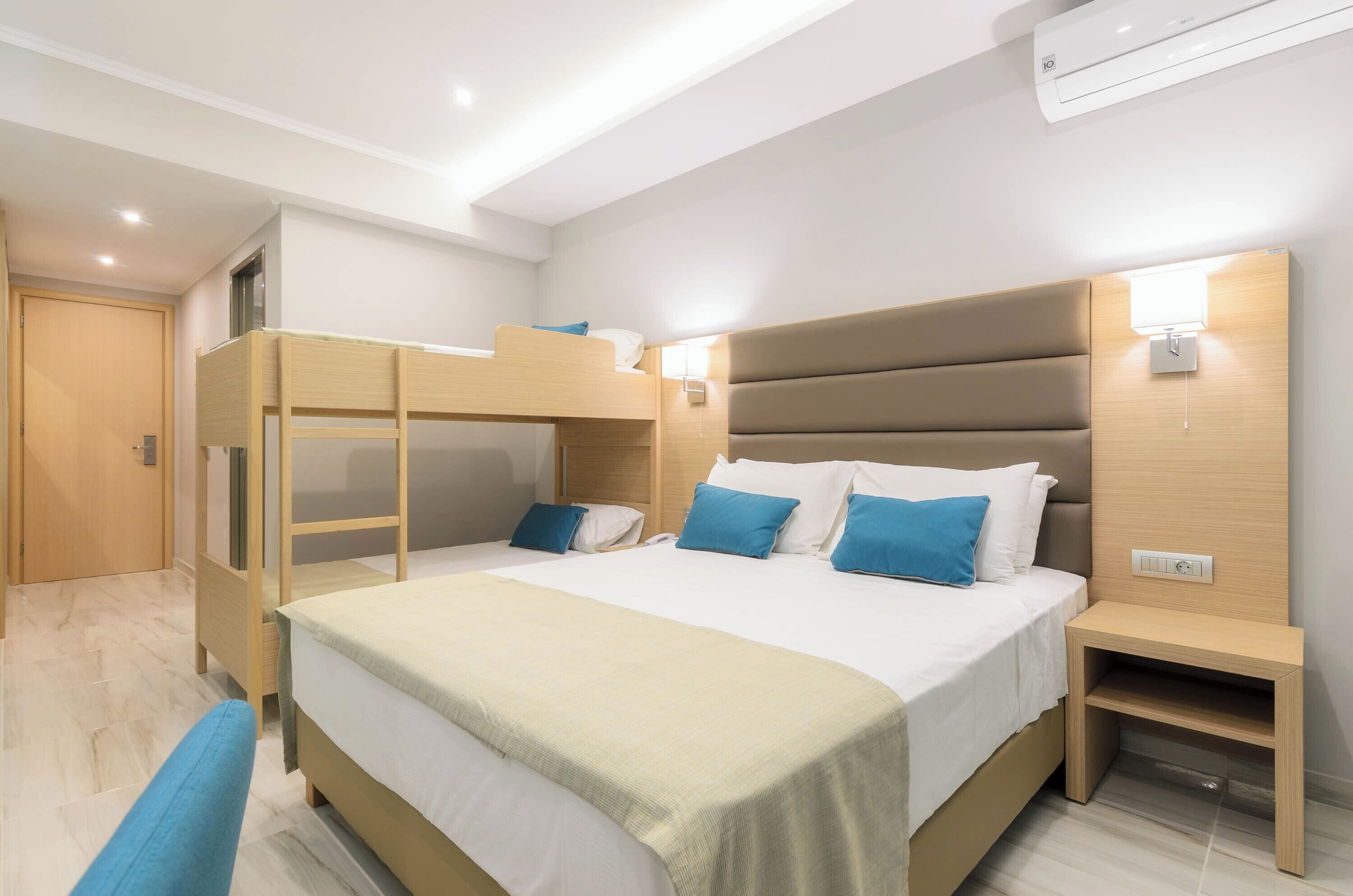 Quarto de hotel moderno com beliche, mesa de cabeceira, luminária de parede e mesa auxiliar.