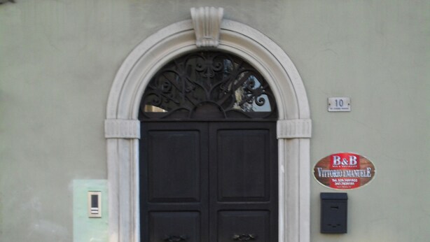 Um edifício com uma porta preta grande e elaborada, dois vasos de plantas de cada lado, e uma placa indicando um estabelecimento chamado B&B.