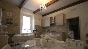 Uma sala de jantar com uma mesa posta para quatro pessoas, um candelabro e uma parede de pedra com um relógio.