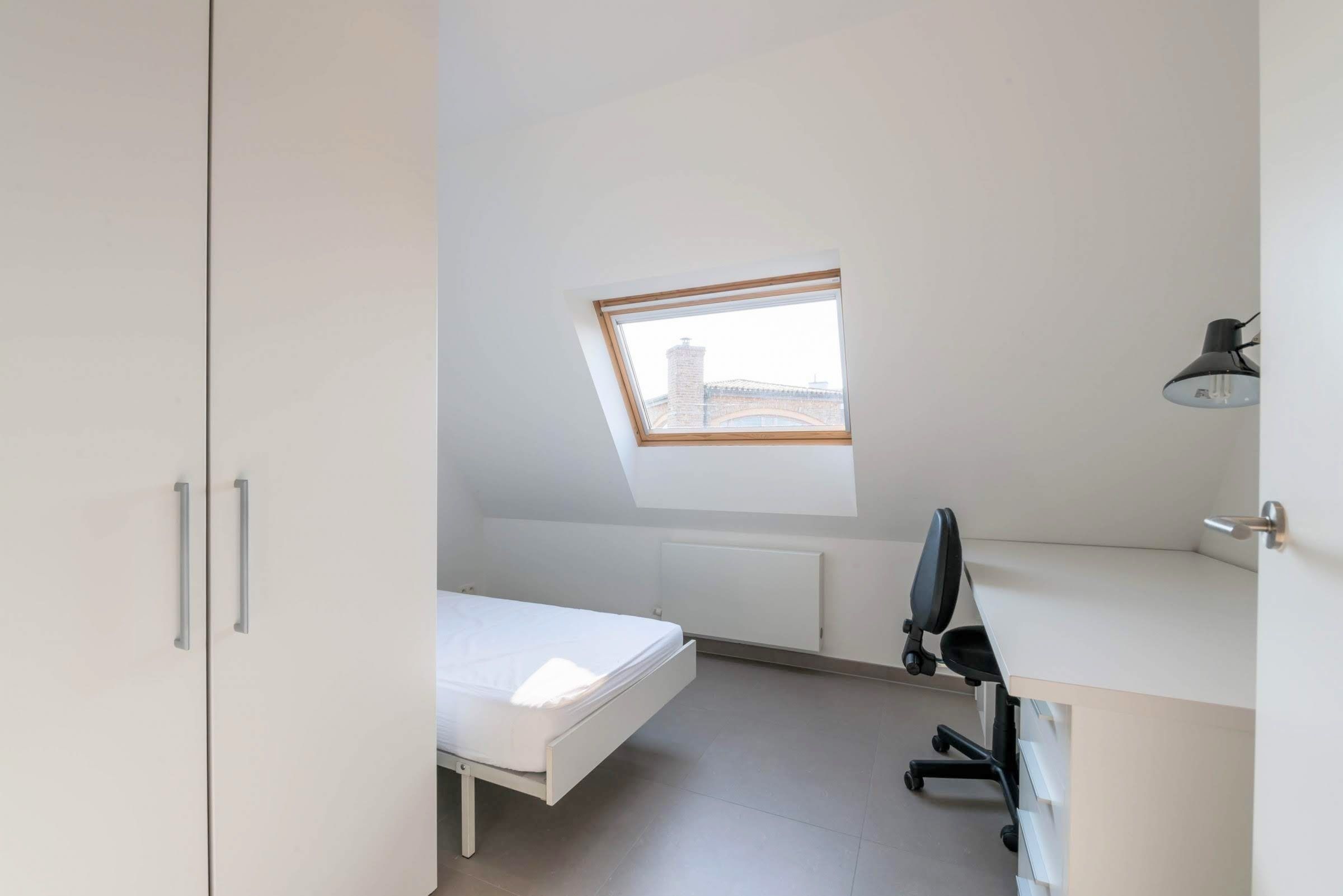 Quarto com claraboia, cama, escrivaninha e cadeira.