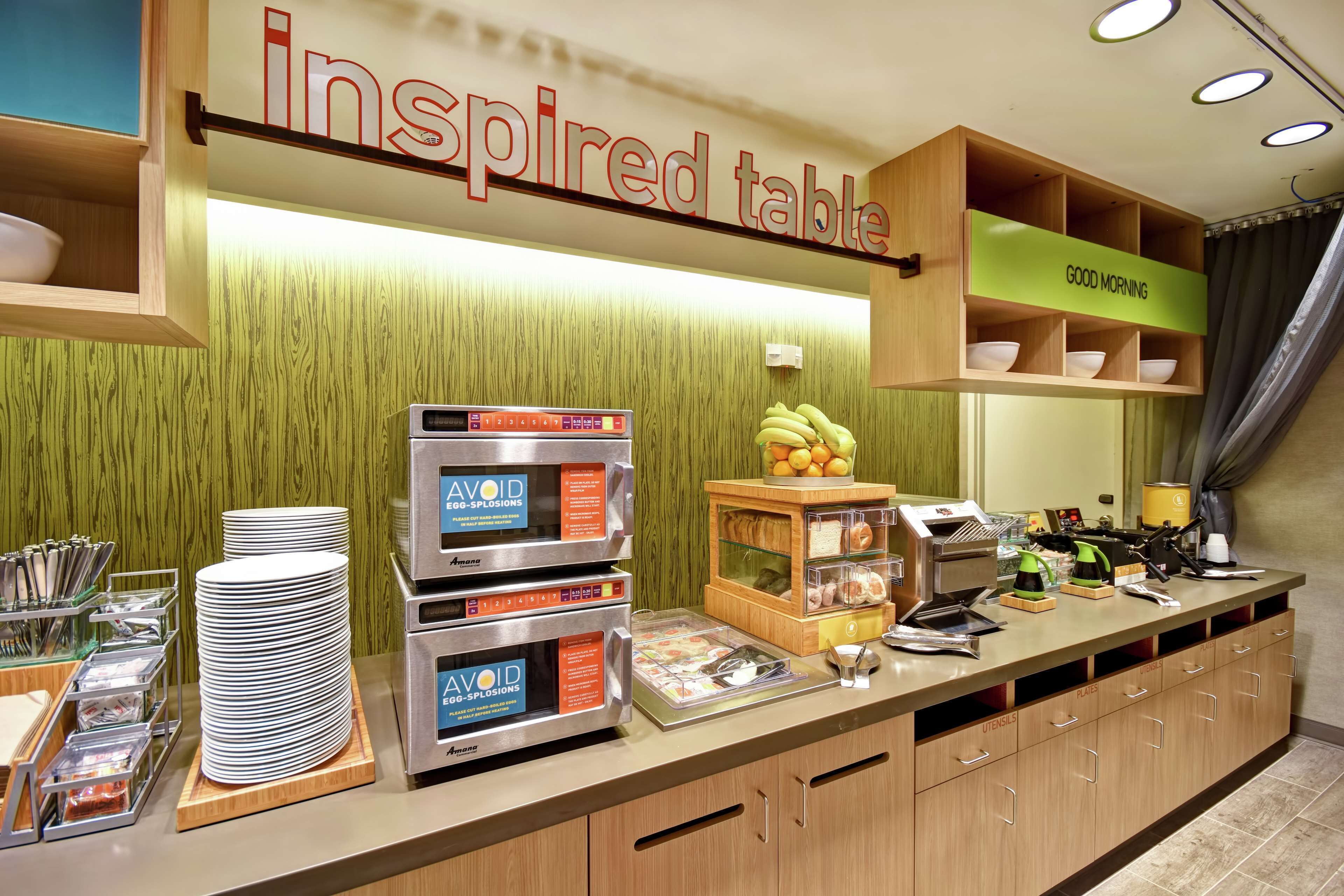 Espaço de buffet de café da manhã com uma placa que diz 'inspired table', uma máquina de café e diversos alimentos.