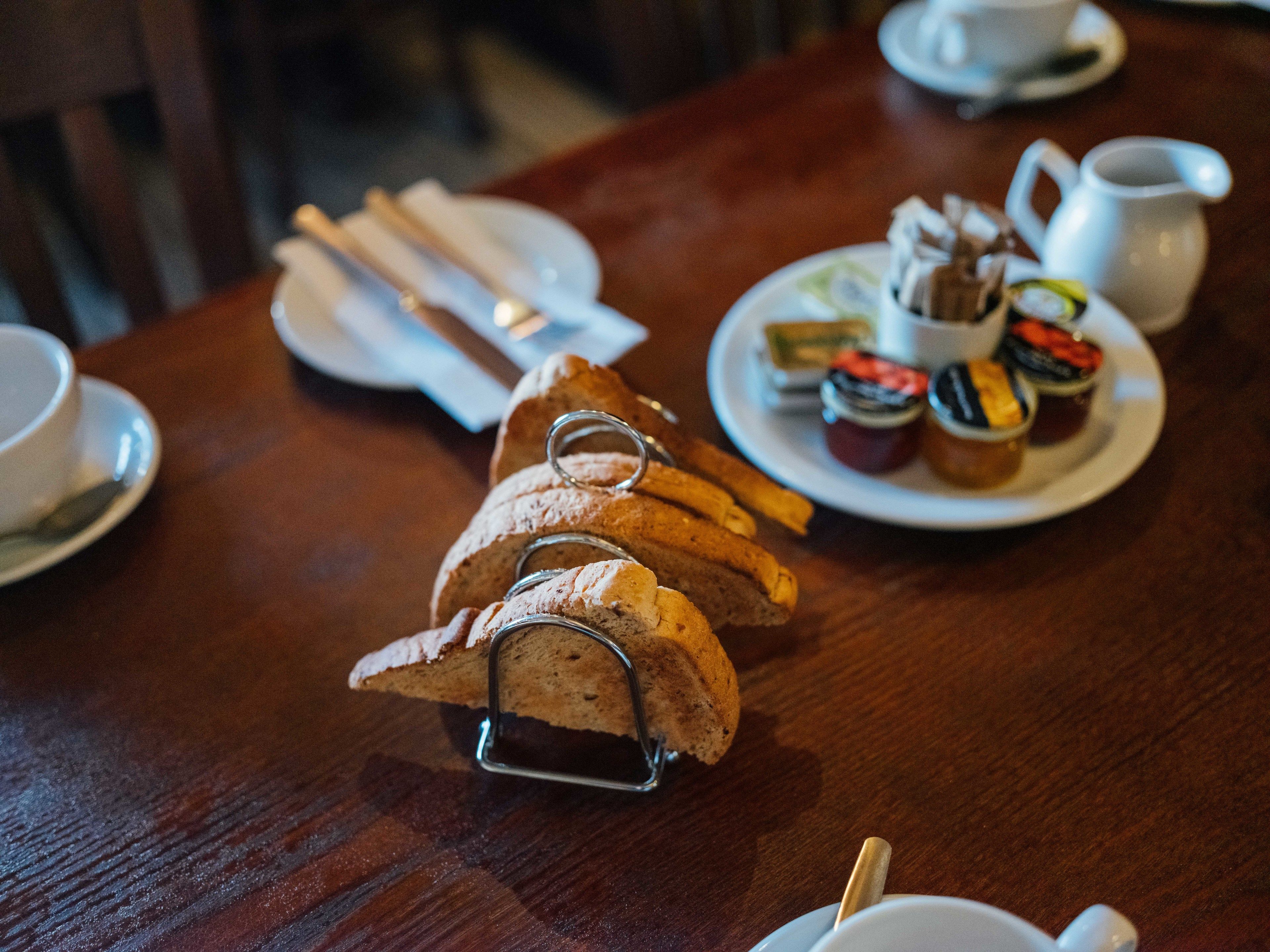 Uma mesa de madeira com um cesto de pão, pratos de pastelaria e uma jarra de água.