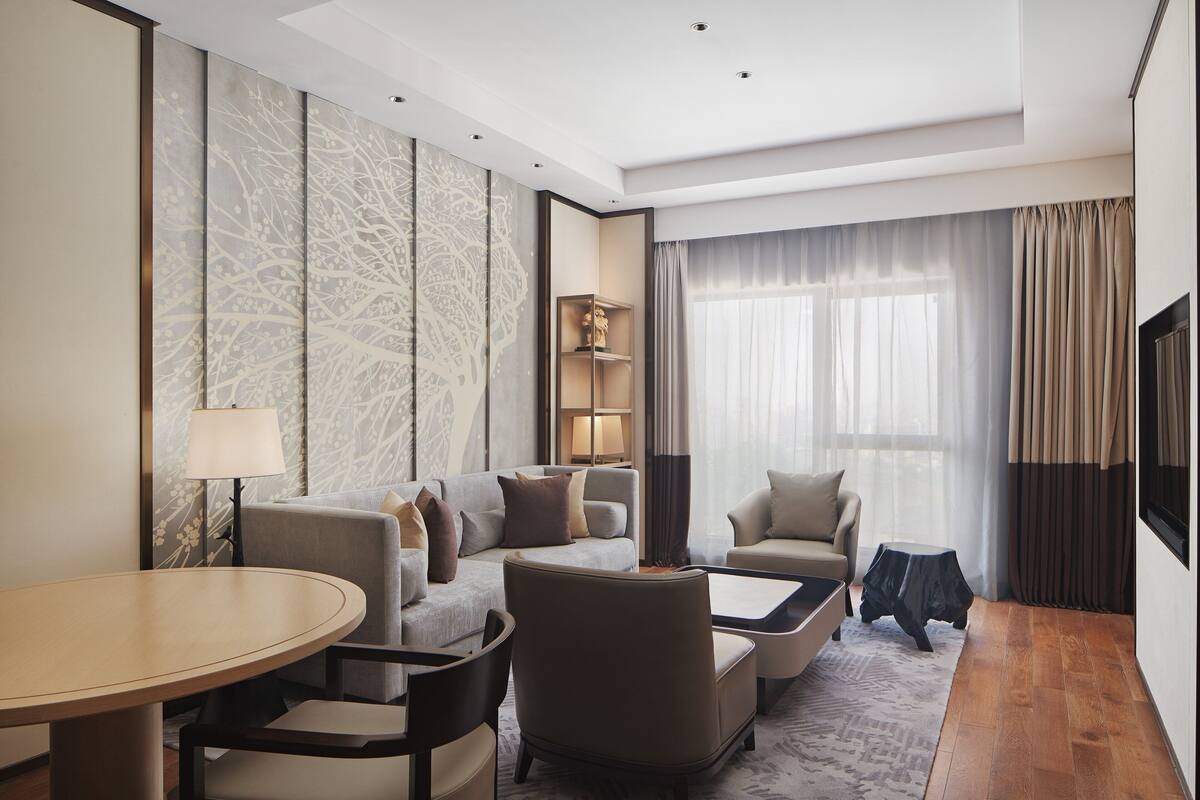 Quarto de hotel moderno com sofá, poltronas, mesa de centro, televisão e luminária.