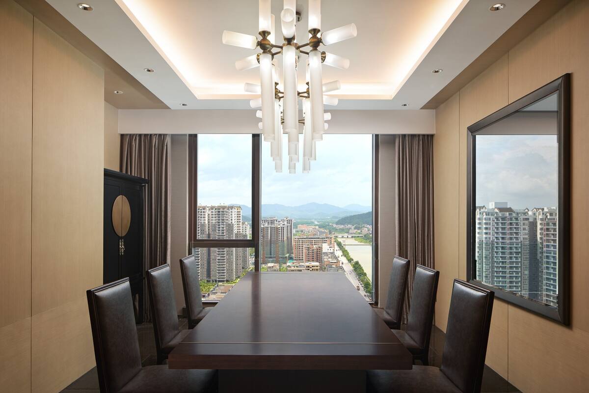 Uma sala de conferências com uma mesa grande e cadeiras, janelas amplas com vista para a cidade e um lustre moderno.