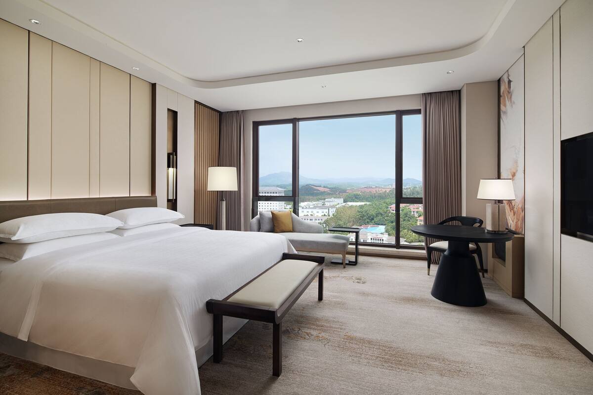 Quarto de hotel moderno com uma cama grande, uma escrivaninha e vista para a cidade.