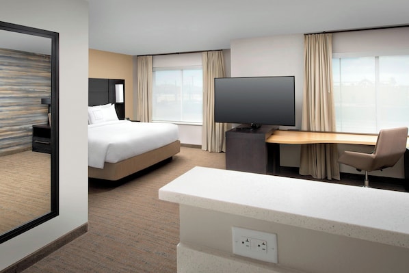 Quarto de hotel com cama, escrivaninha, televisão e cadeira.