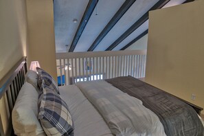 Quarto com teto inclinado, cama com várias almofadas e vista para a varanda.