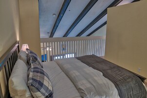 Quarto com teto inclinado, cama com várias almofadas e vista para a varanda.