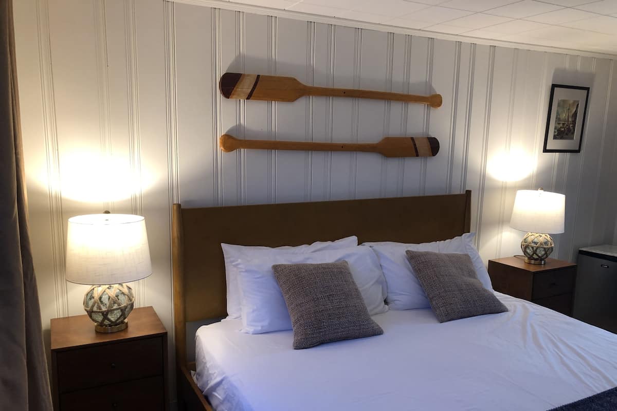 Cama bem arrumada com lençóis brancos e duas almofadas, com duas mesinhas de cabeceira de madeira e abajures.